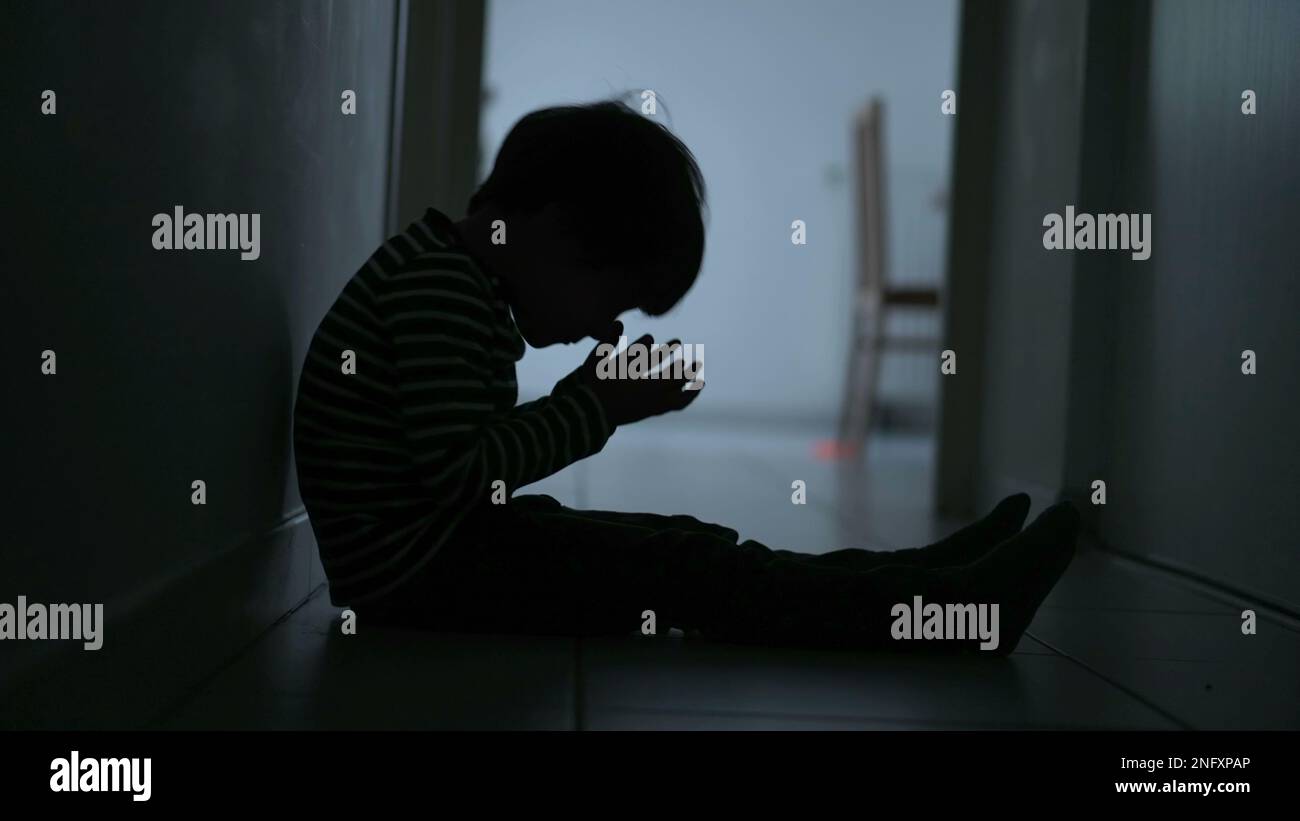 One scared desperate child covering face in fear sitting in dark ...