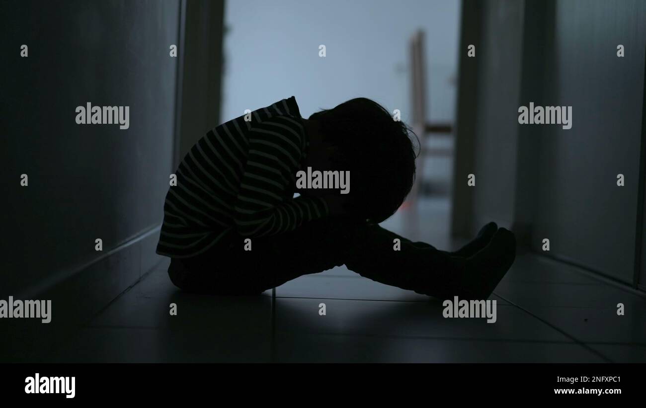 One scared desperate child covering face in fear sitting in dark ...
