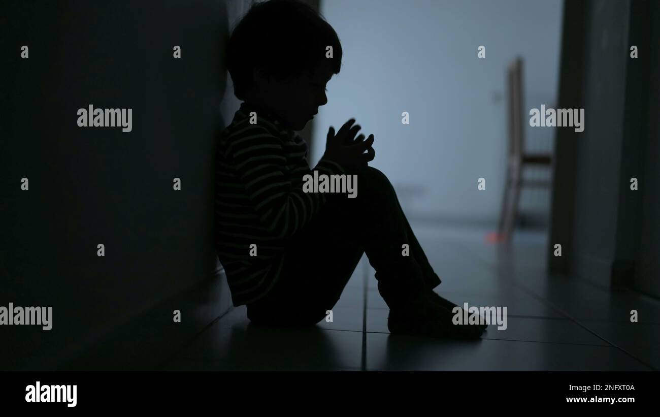 Small child covering face feeling despair. One small boy sitting in dark hallway corridor at ...