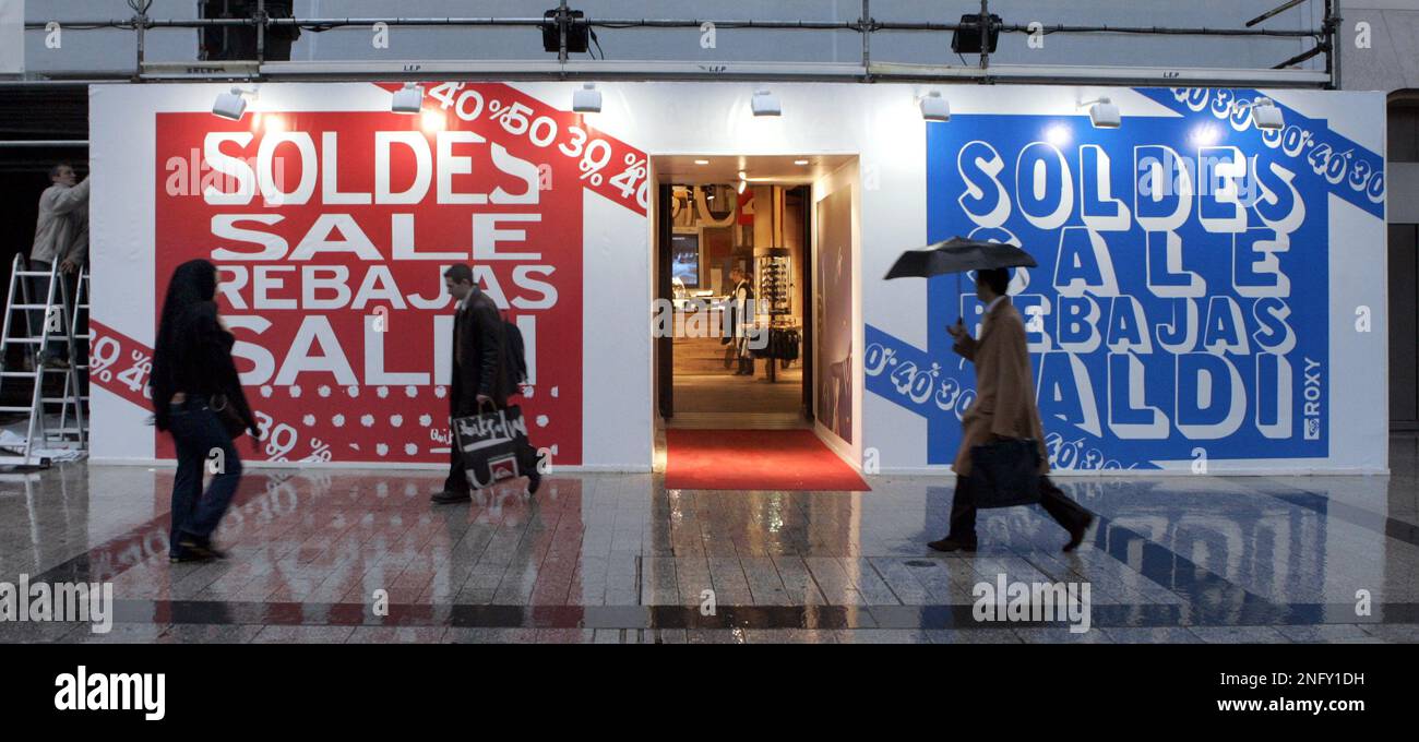 People pass a shop on the Champs Elysees, with a discount signs ...