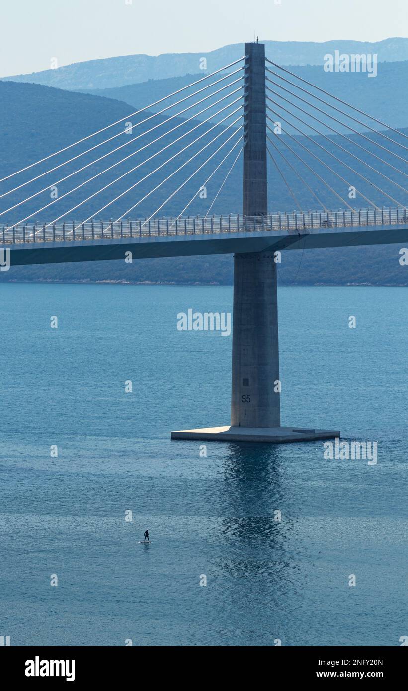 A beautiful vertical view of a surfer and Peljesac Bridge on a sunny ...