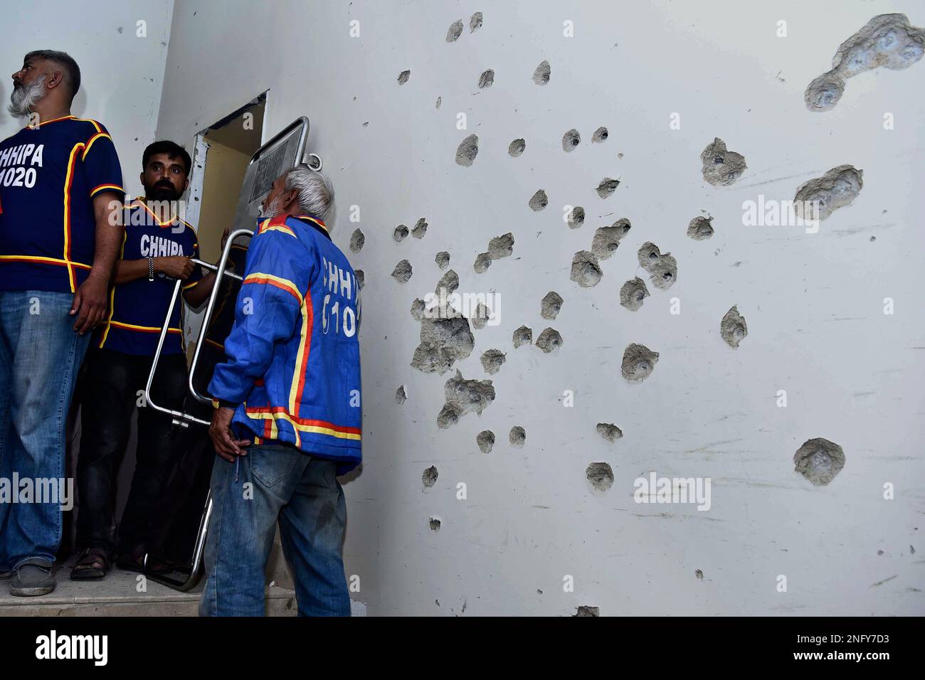 Rescue workers stand beside a bullet-riddled wall after security forces ...