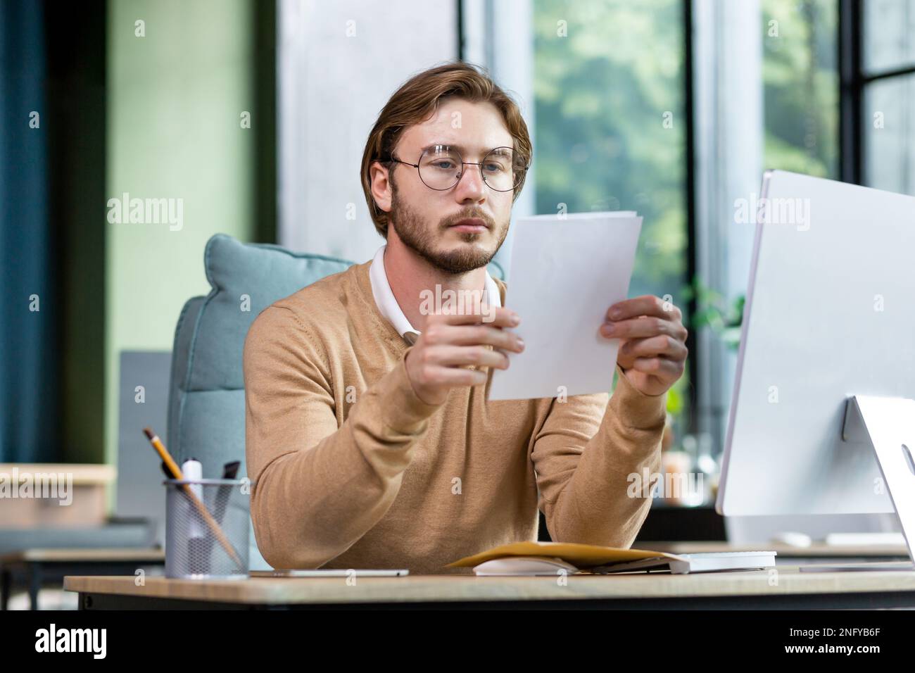 A serious young man businessman, freelancer, programmer sits at a desk ...