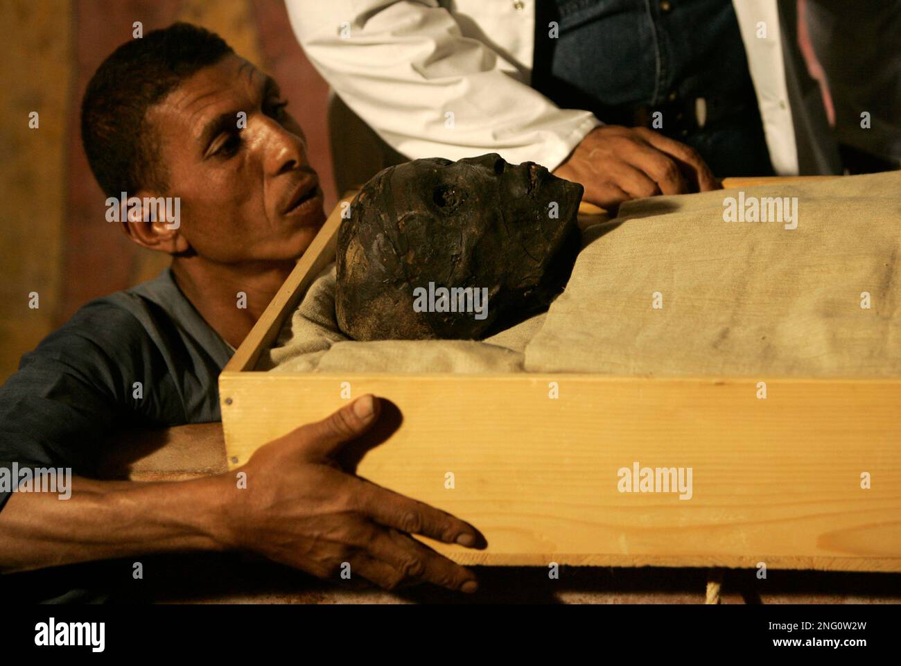 An archeological worker looks across at the face of the linen-wrapped ...