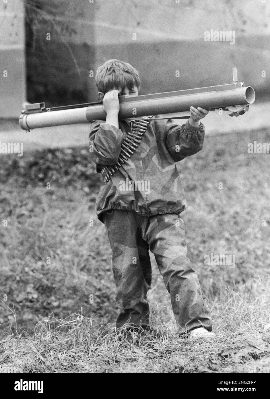 A young boy wears a cartridge belt while playing with a used hand-held ...