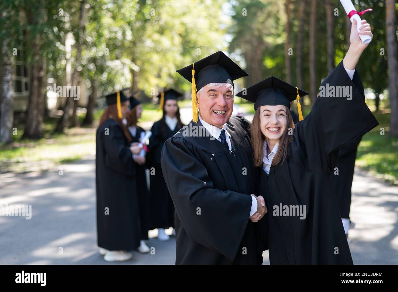 A group of graduates in robes outdoors. An elderly man and a young ...