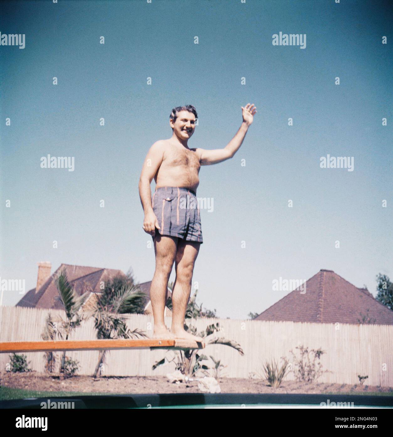 Entertainer Liberace, wearing swimsuit, stands on his diving board at ...