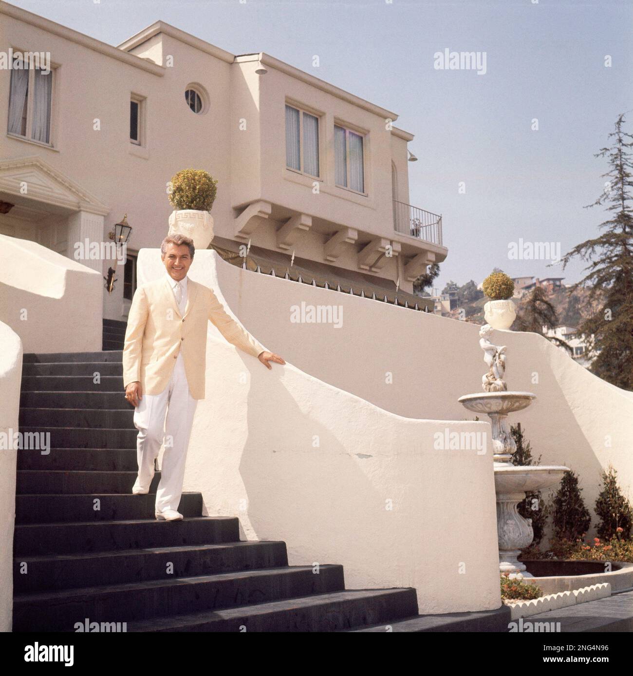 Entertainer Liberace walks down the stairs from the stone balcony area ...