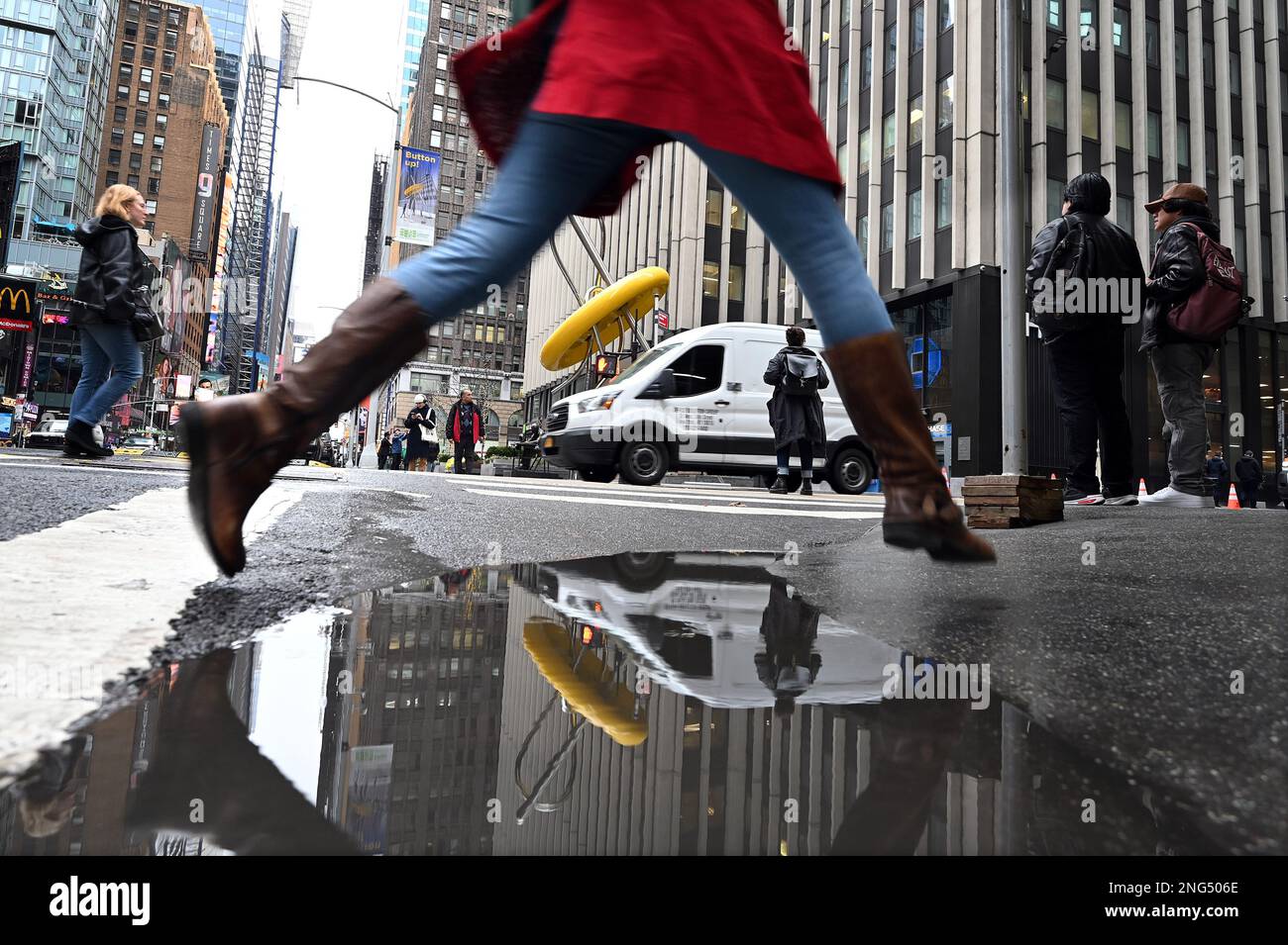 New York, USA. 17th Feb, 2023. A woman leaps over a rain puddle ...