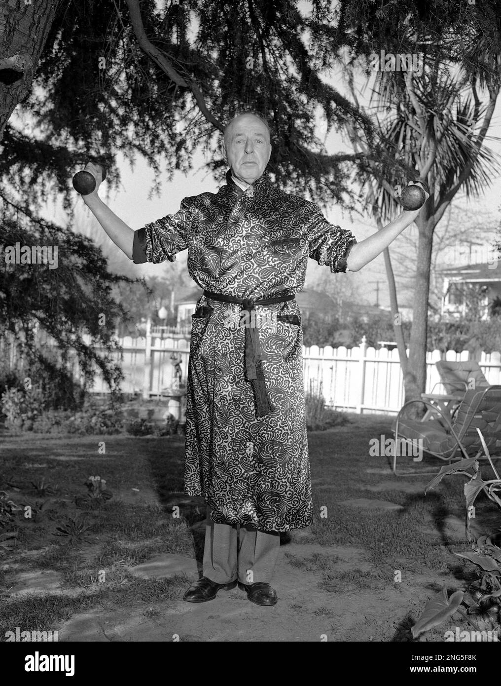 D.W. Griffith, wearing a robe, lifts dumbbells in the yard of his ...