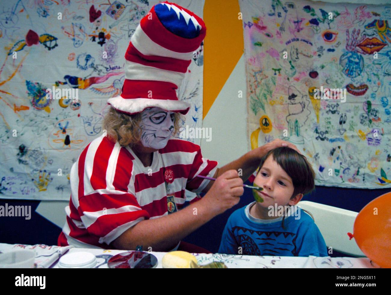 Wavy Gravy, costumed as The Cat in the Hat, paints the face of 5-year ...