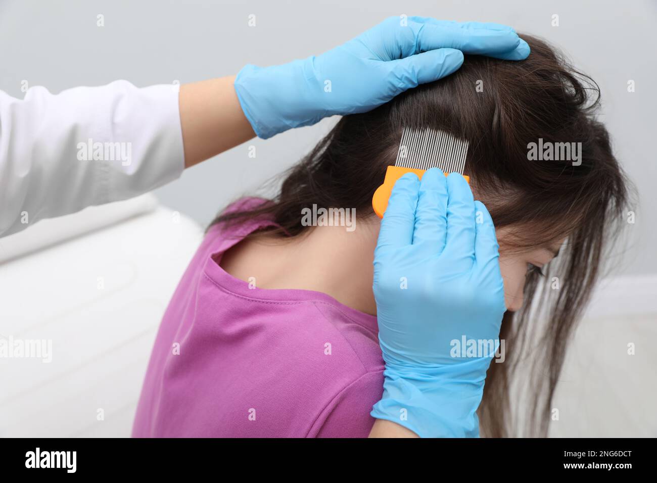 Doctor using nit comb on little girl's hair indoors. Anti lice ...