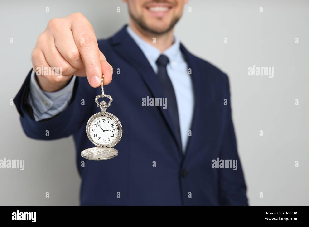 Happy businessman holding pocket watch on grey background, closeup ...