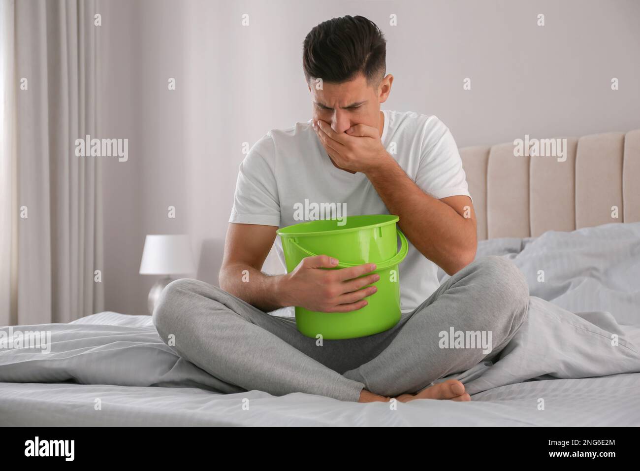 Man with bucket suffering from nausea on bed at home. Food poisoning ...