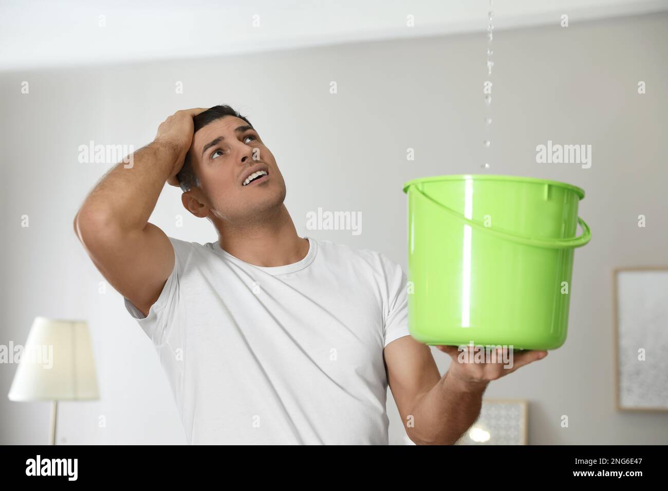 Emotional man collecting water leaking from ceiling in living room ...