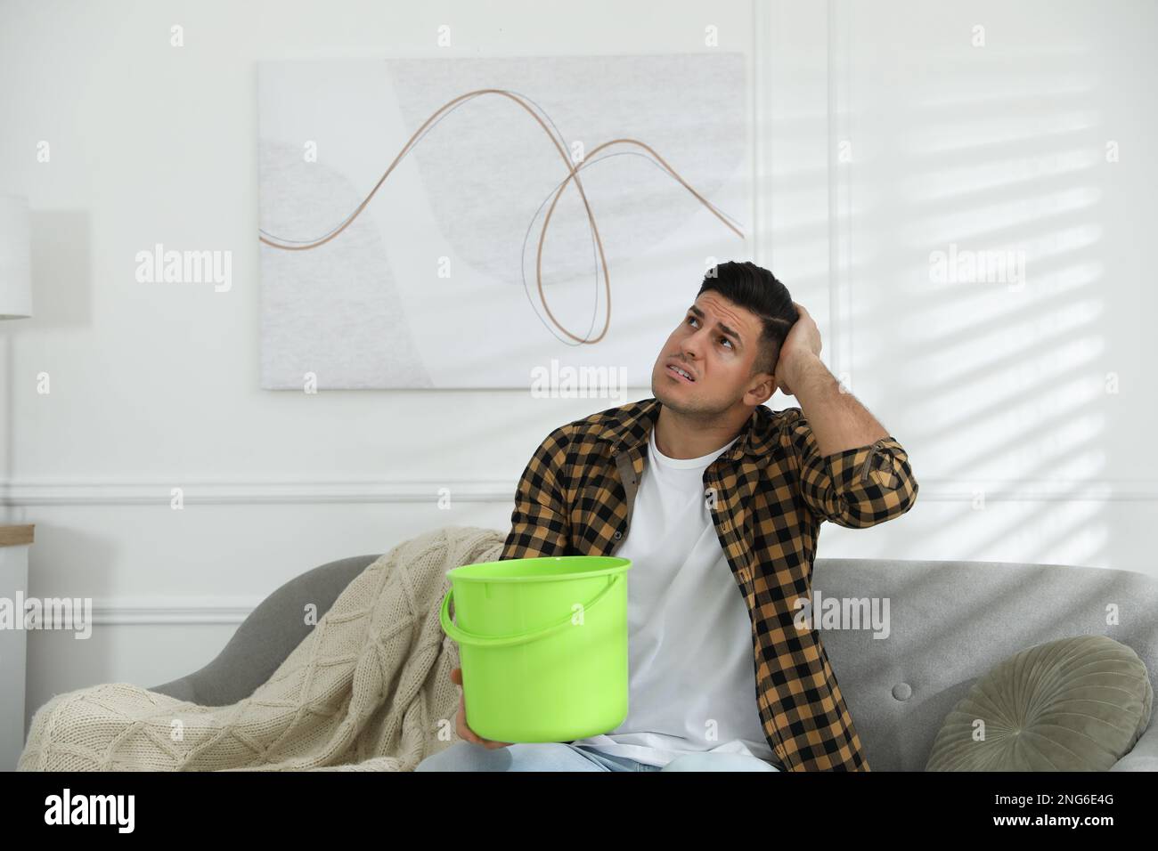 Emotional man collecting water leaking from ceiling in living room ...