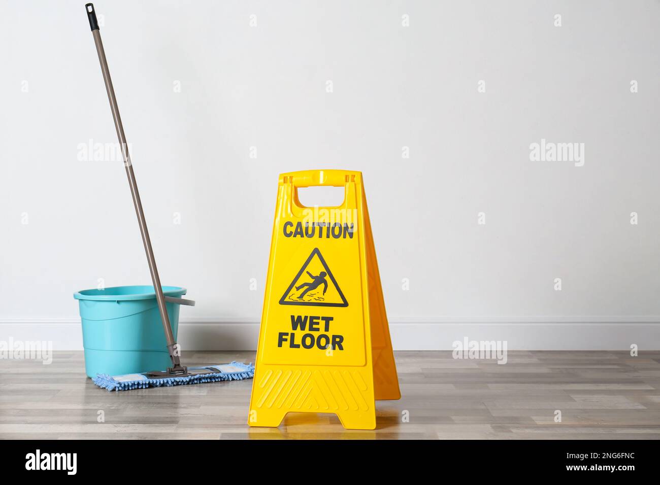 Safety sign with phrase Caution wet floor, mop and bucket indoors ...