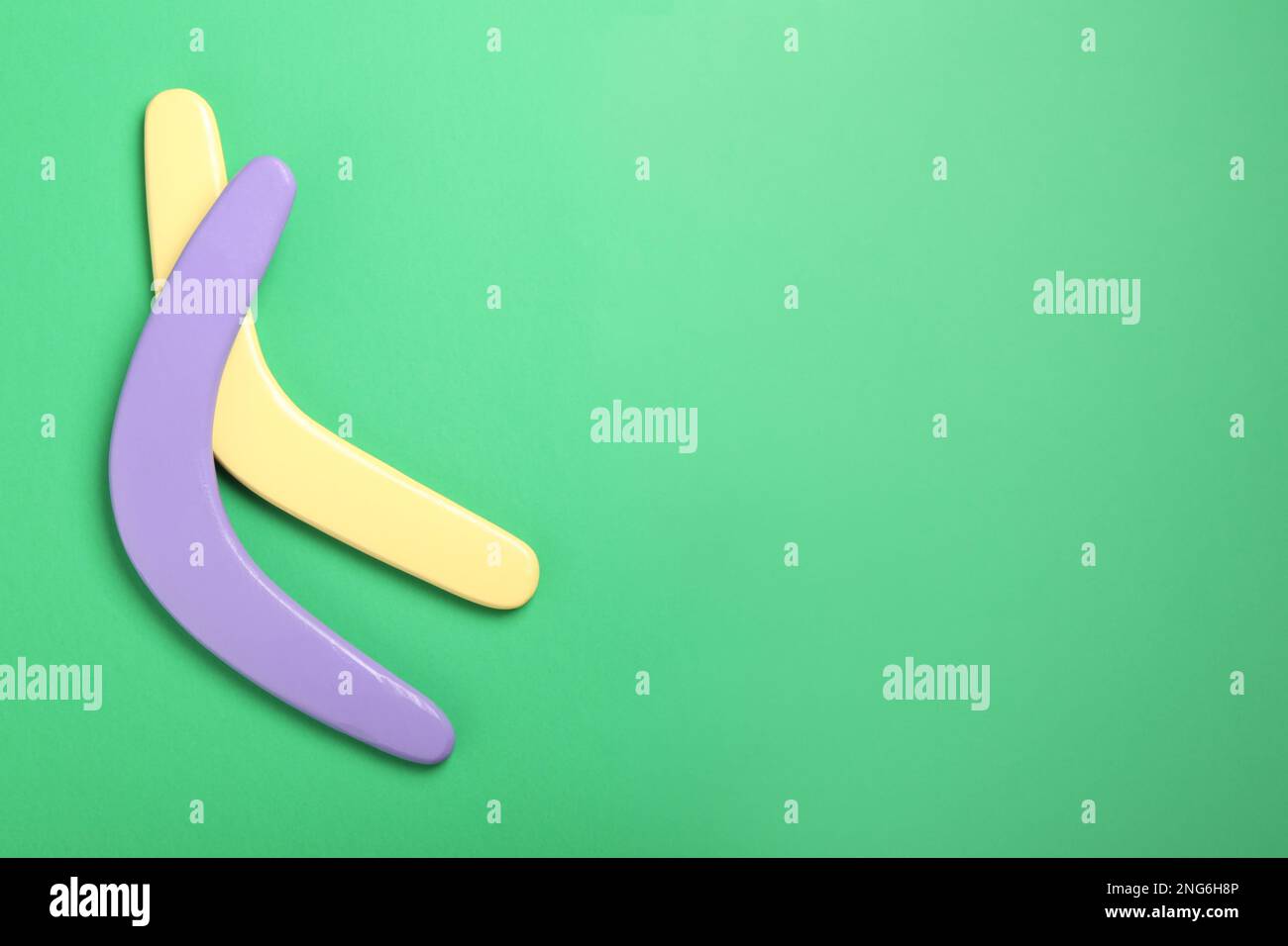 Colorful wooden boomerangs on green background, flat lay. Space for ...