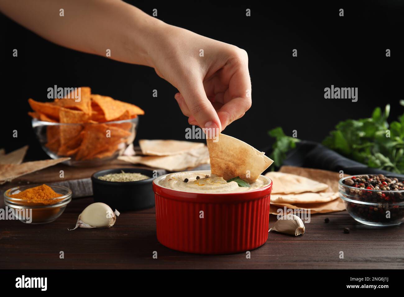 Woman dipping pita chips into hummus at wooden table, closeup Stock ...