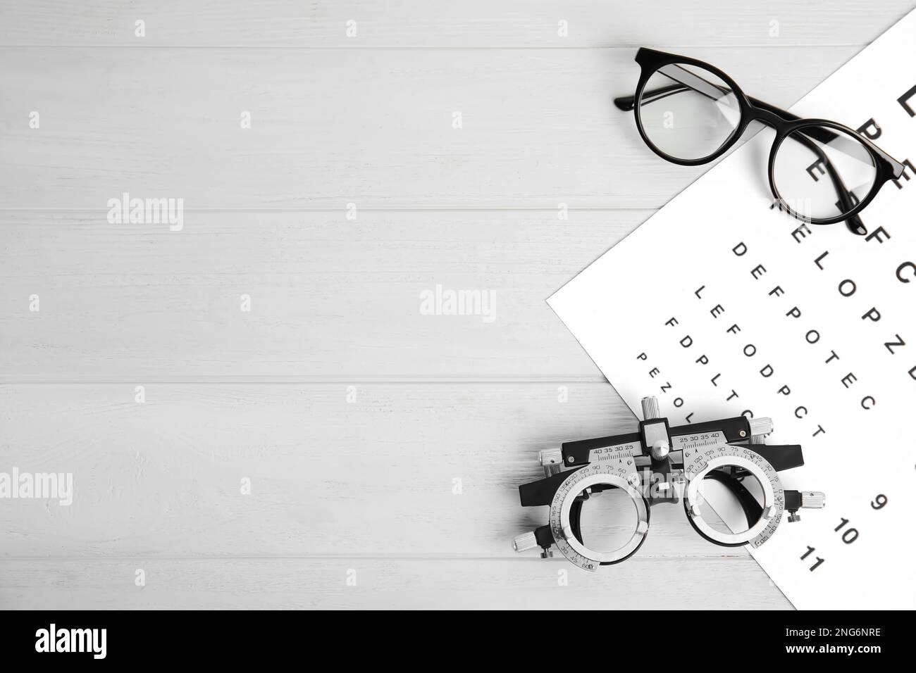 Trial frame, eye chart test, glasses and space for text on white wooden ...