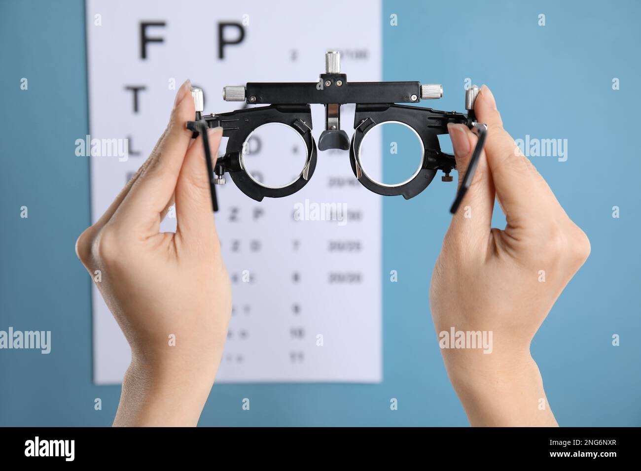 Woman holding trial frame against eye chart test on blue background ...