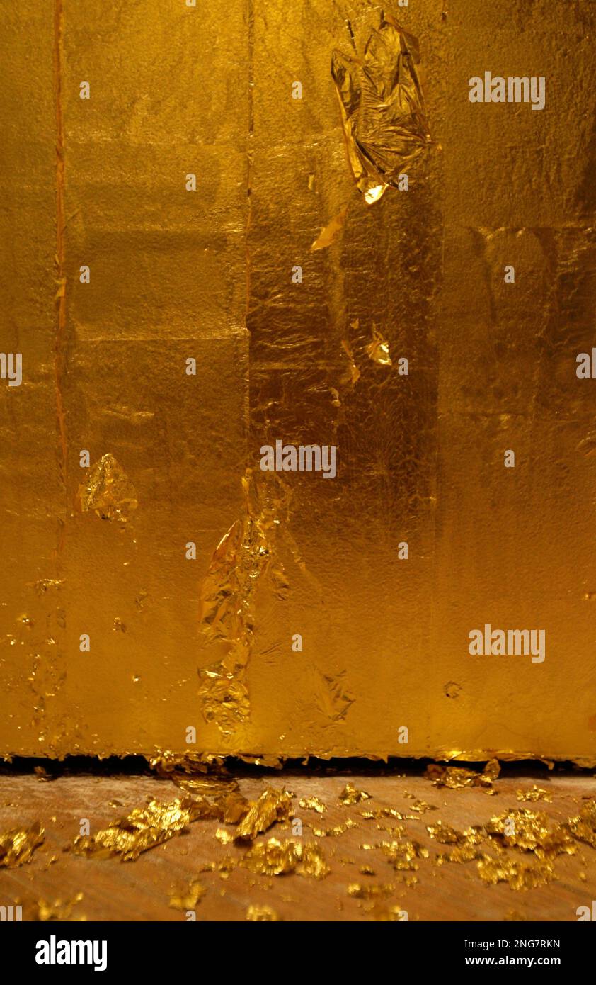 Gold flakes rest on the floor below a wall covered in gold as part of a ...