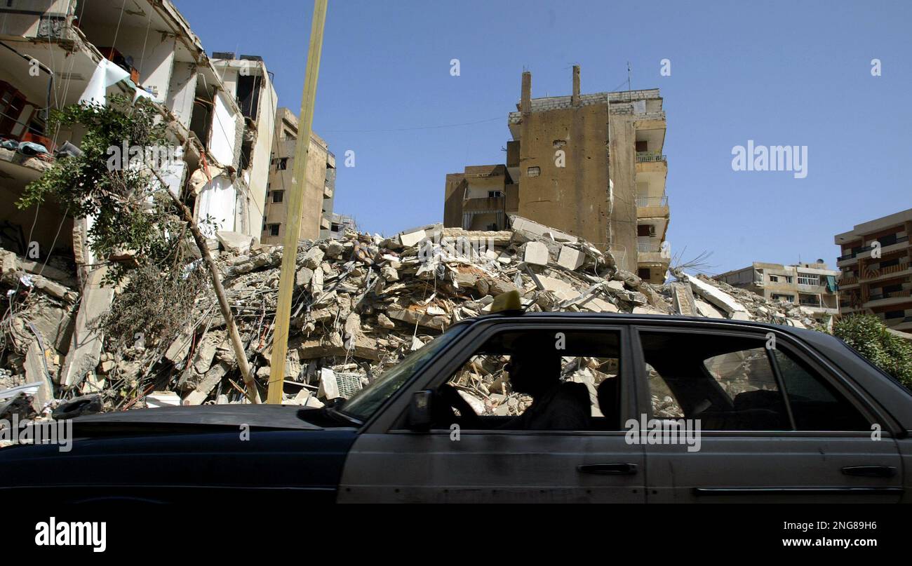 A Lebanese taxi driver drives past the rubble of a collapsed apartment ...