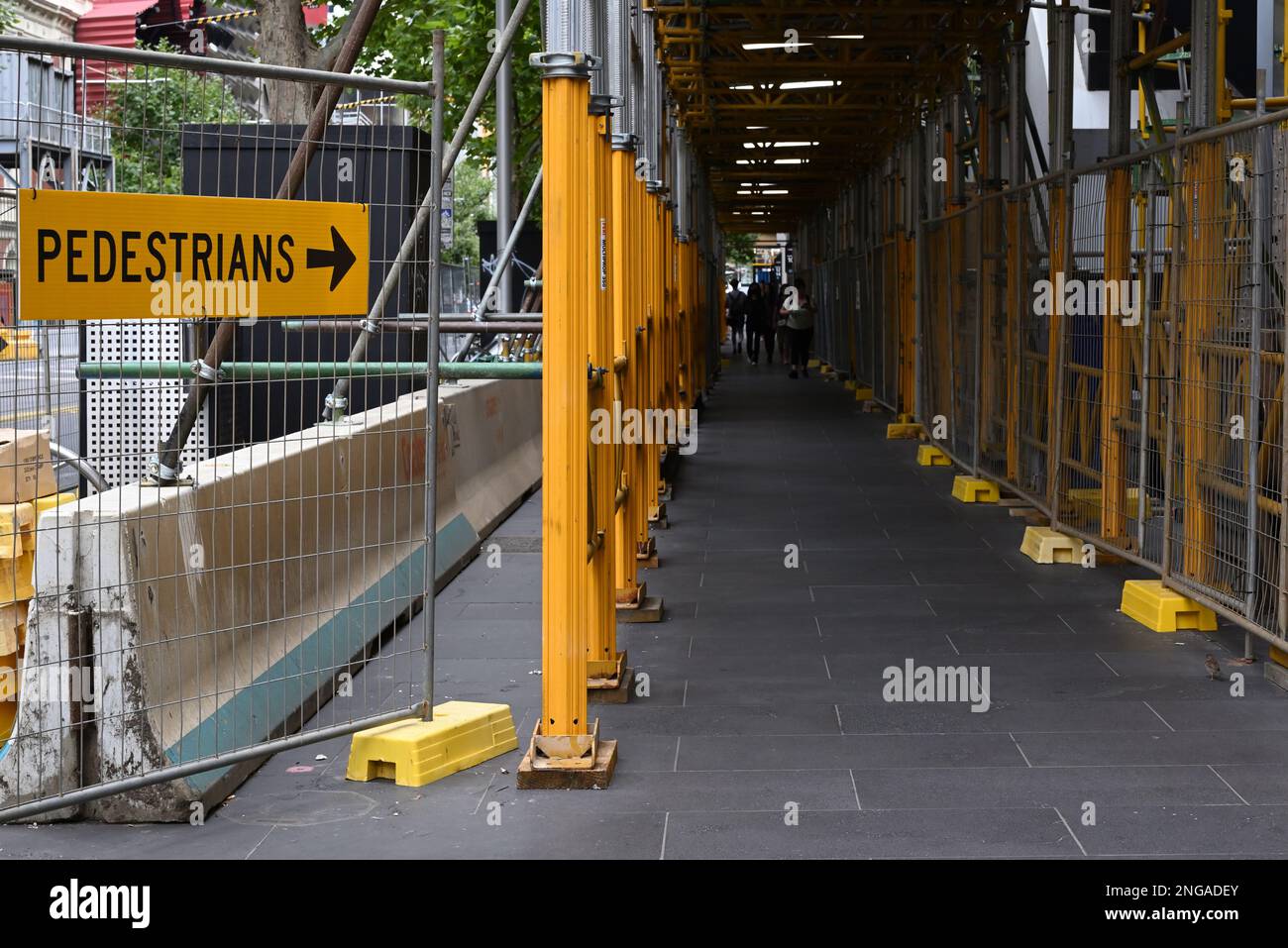 Yellow pedestrians sign on a temporary fence pointing people to walk ...