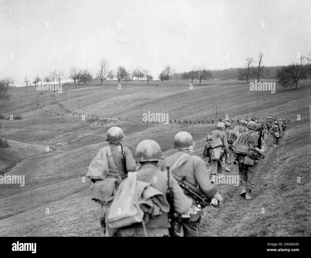 U.S. infantrymen march in an endless stream over hilly countryside ...