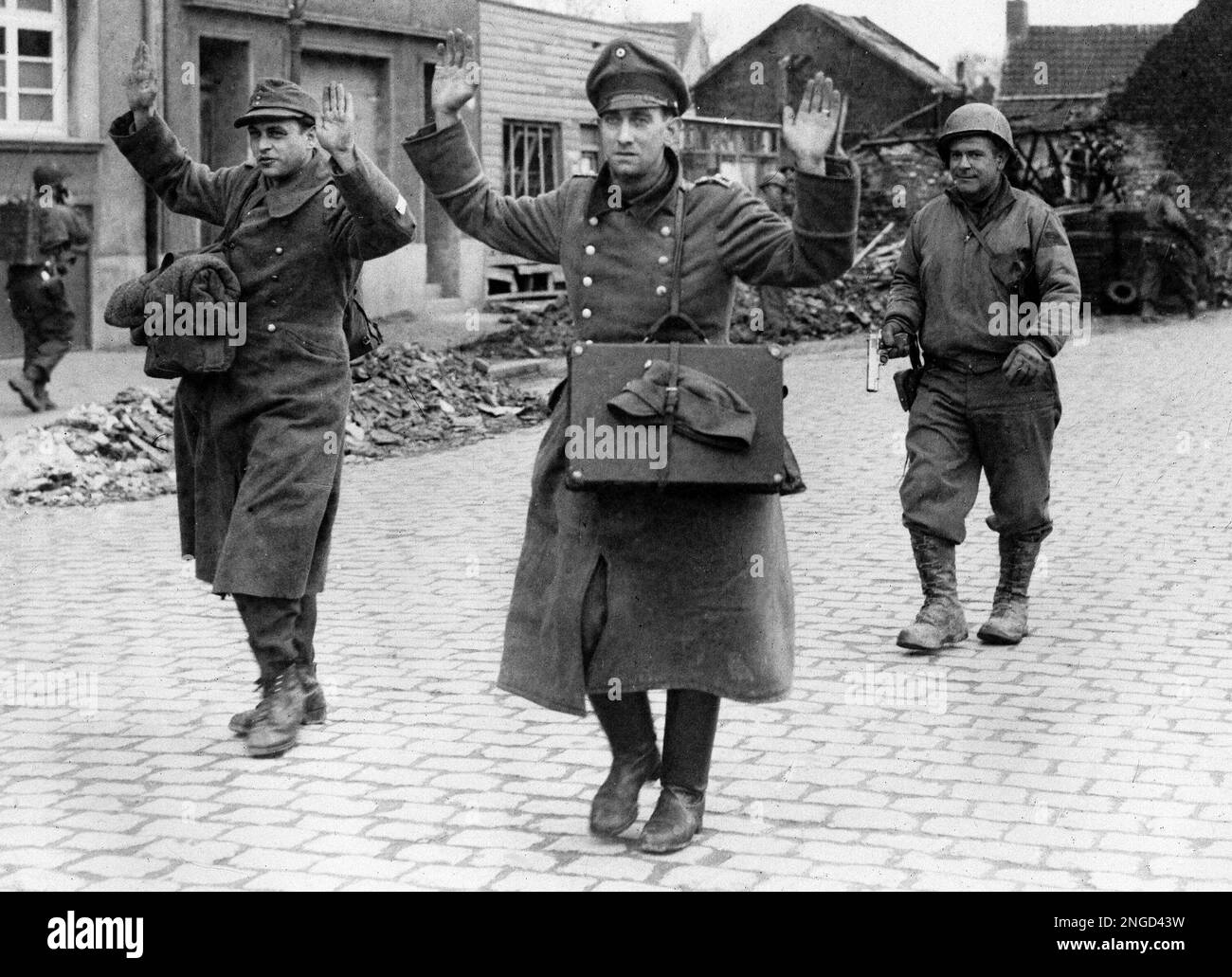 Two German soldiers, with their hands raised, are marched down a street ...
