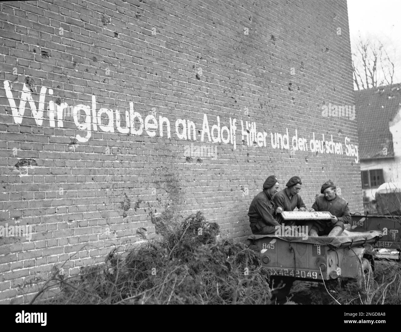 Three British soldiers examine a street sign as they sit under a wall ...