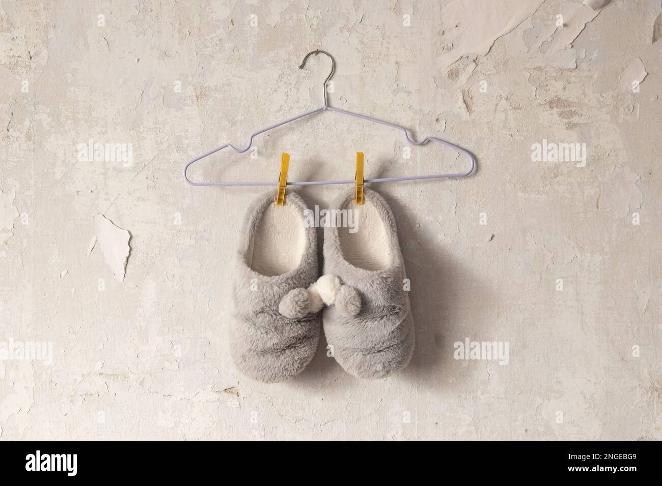 gray soft female room slippers hanging on a hanger on an old white wall ...