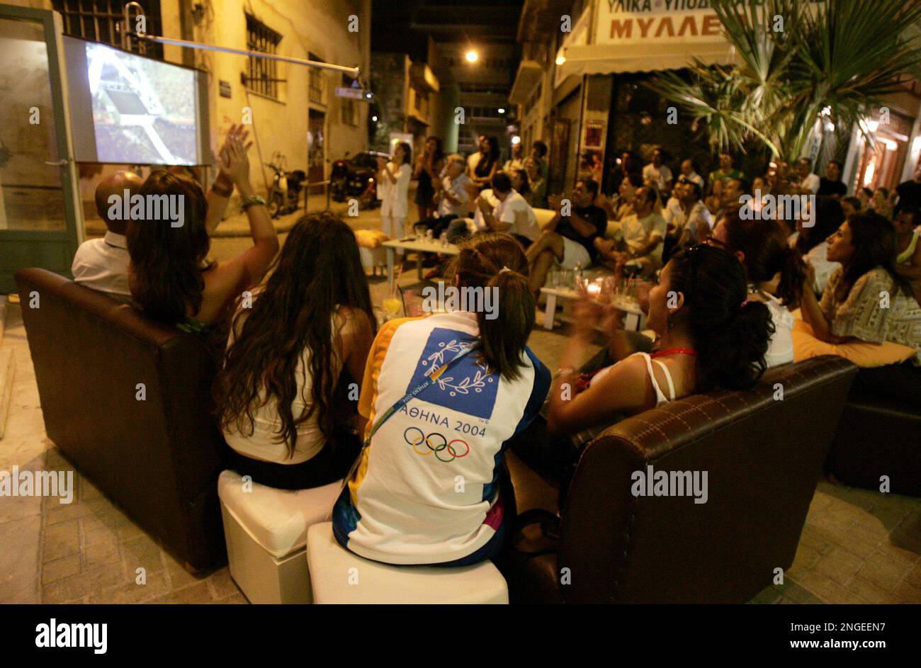 A group gathers around a television screen showing the opening cermony ...