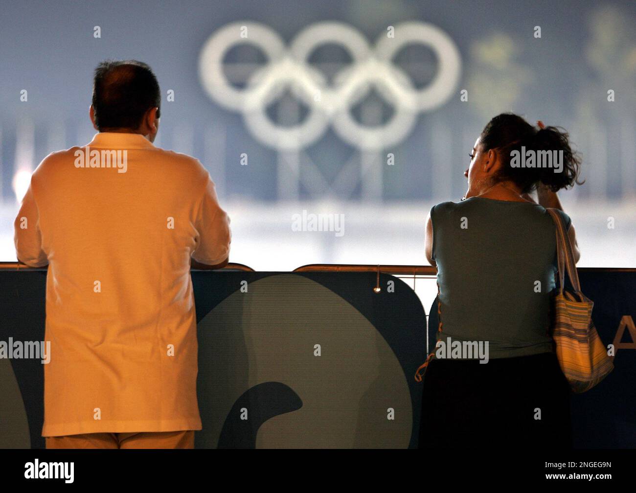 A Greek couple stops in front of a sign with the Olympic rings in the ...