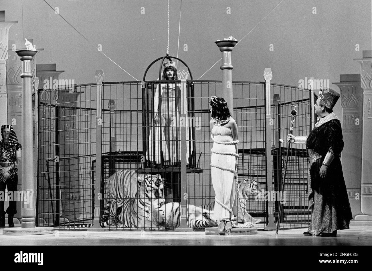Magician Doug Henning, standing on a platform, is lowered into a cage ...