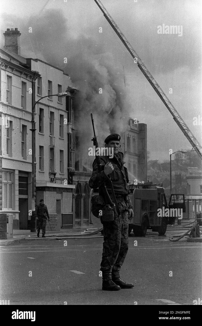 An armed British soldier stands guard outside a burning tea house in ...