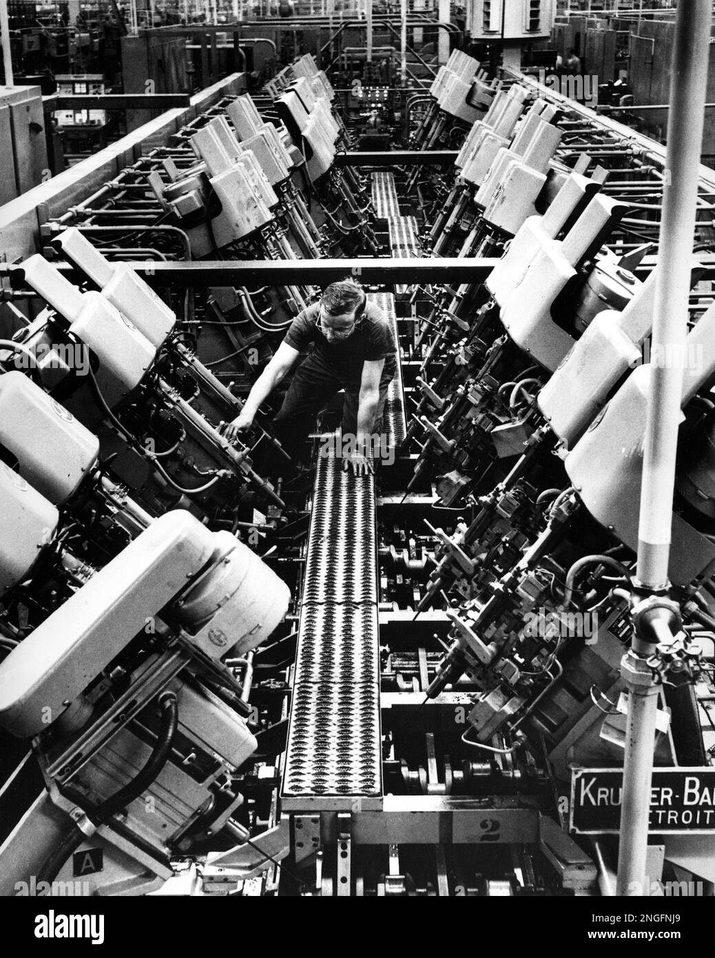 A single worker is shown at a complex, automated machine tool, which ...