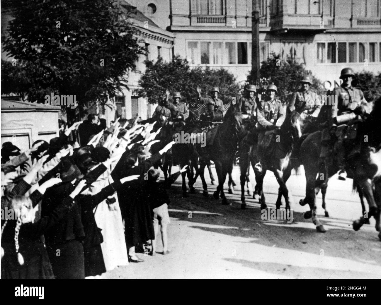 Bystanders render the Nazi salute as German cavalry troops on horseback ...