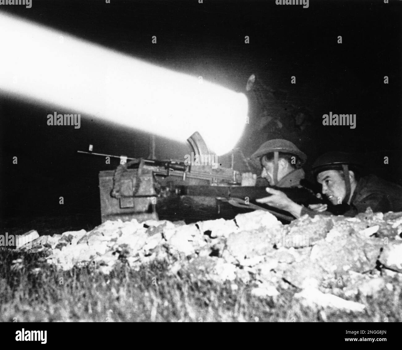 With a searchlight beam piercing through the night, a machine gunner ...