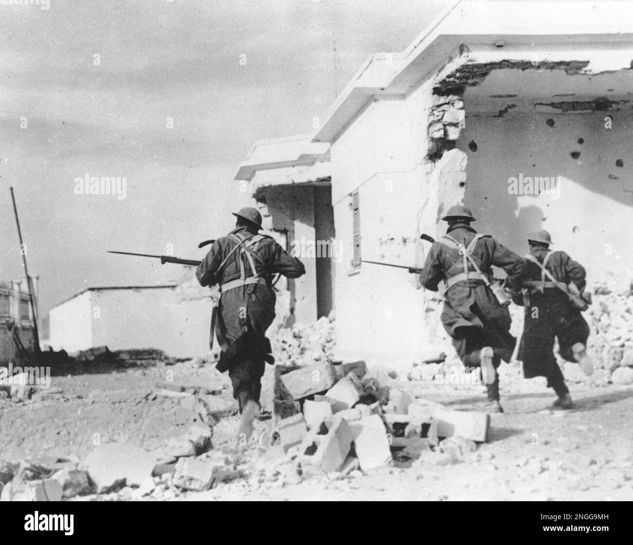 British soldiers dash past shelled buildings and debris in a street at ...