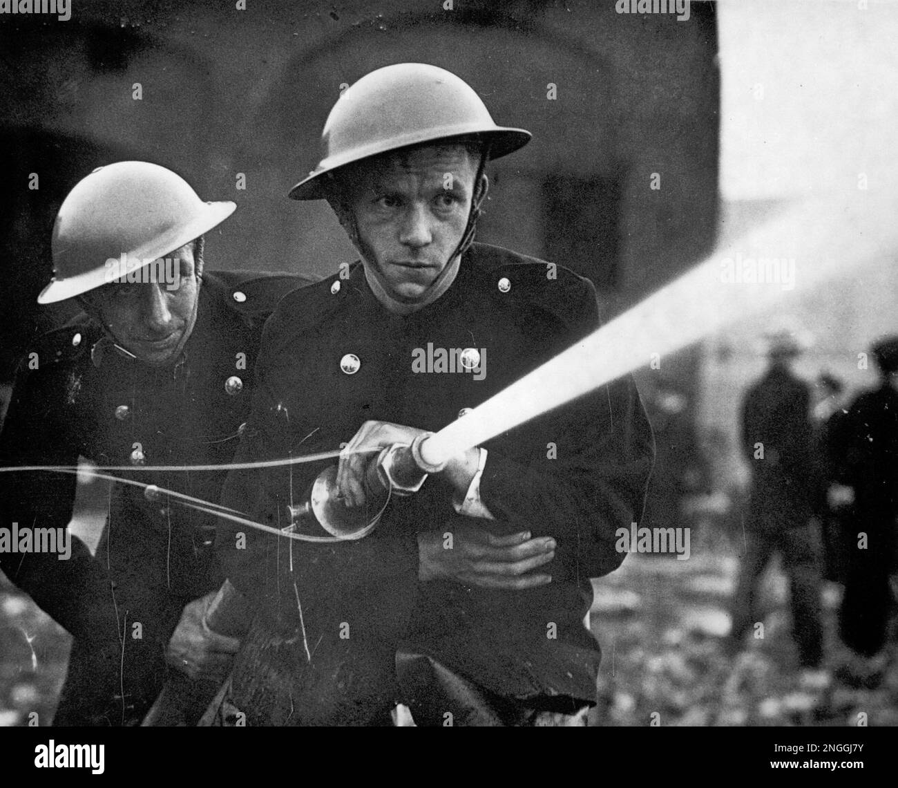 Two firefighters are directing a hosepipe on to the fire, during war ...