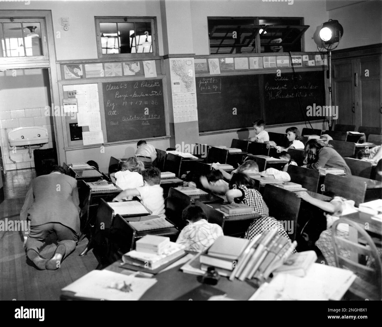 Sixth grade students crouch under or beside their desks along with ...