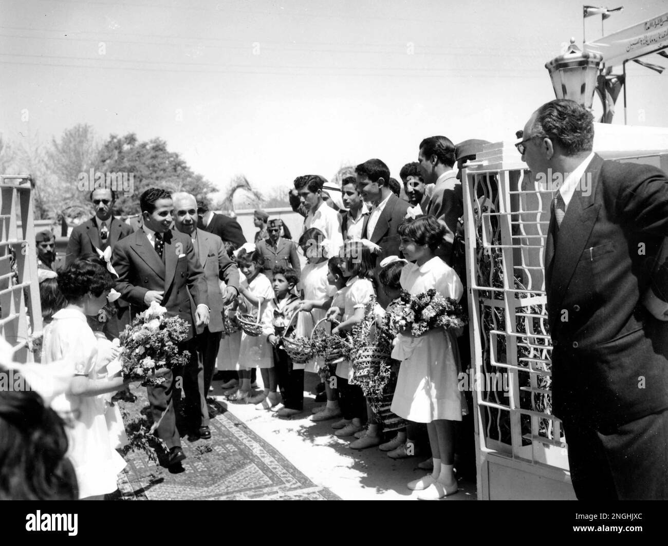 King Faisal II of Iraq walks along a carpet as school children throw ...