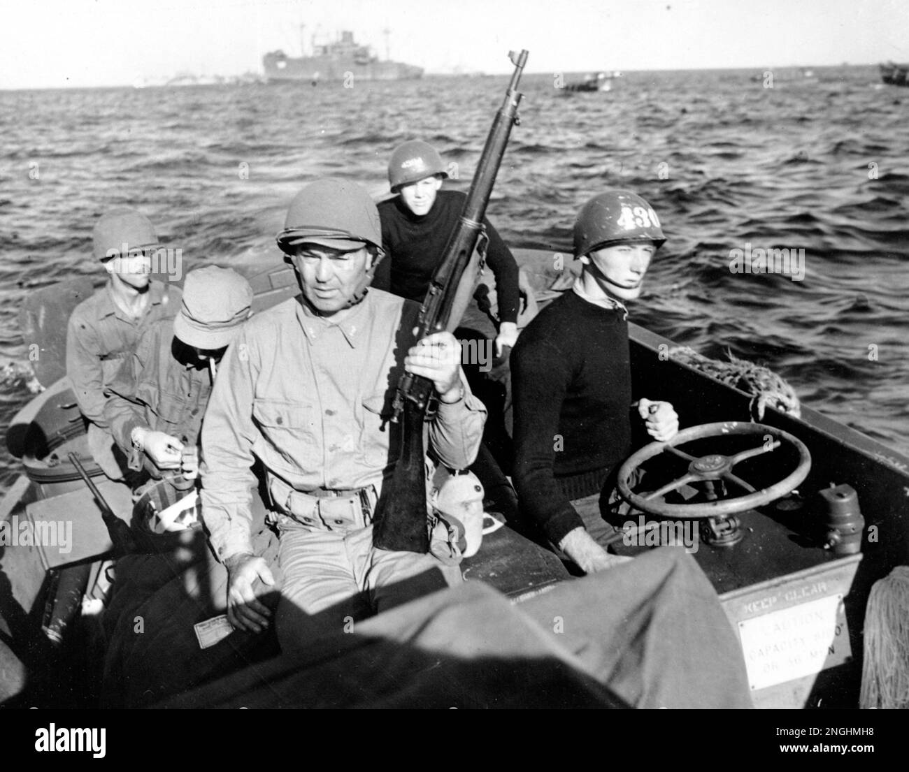 Commander Jack Dempsey, holding rifle, rides a Coast Guard landing ...