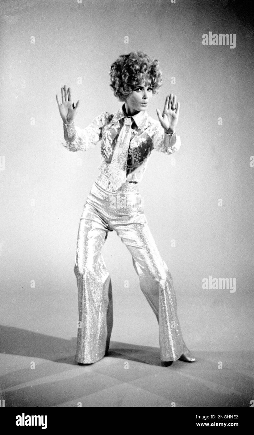 A model wearing a blond wig poses in shiny bell-bottom pants with ...