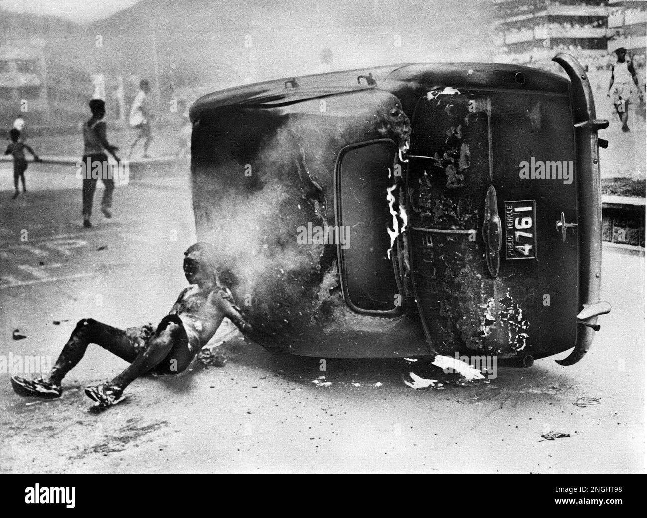 A rioter lies burning next to a car lying on its side after a protest ...