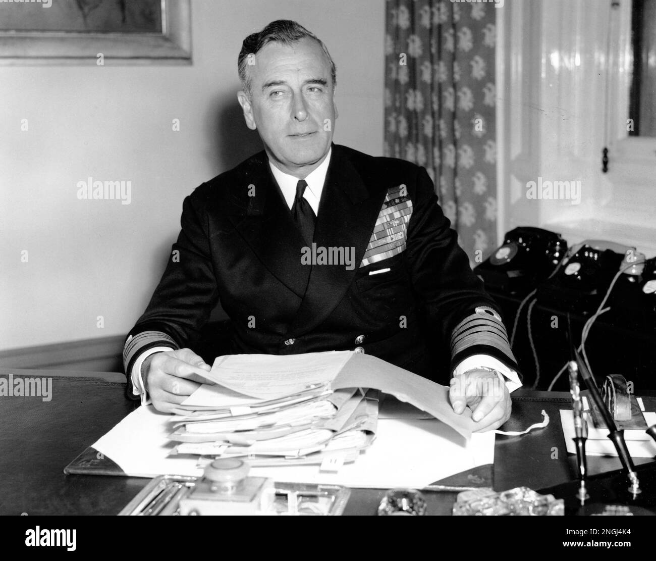 British Admiral Earl Louis Mountbatten sits at his desk in full uniform ...