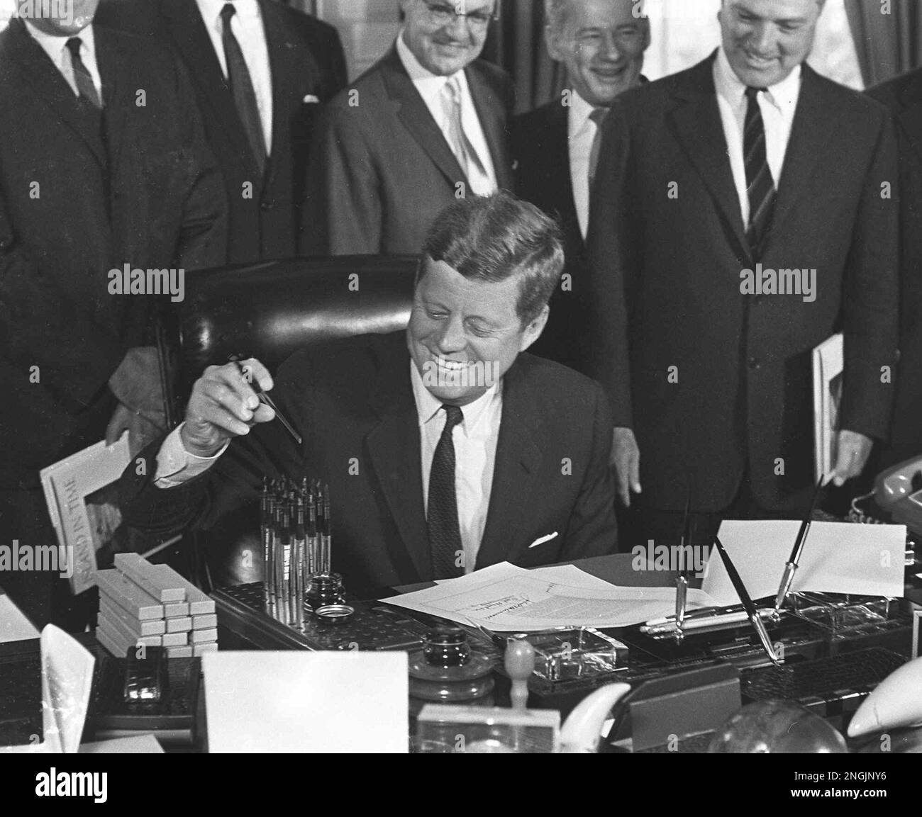 President John F. Kennedy lifts a pen from a rack on his office desk as ...