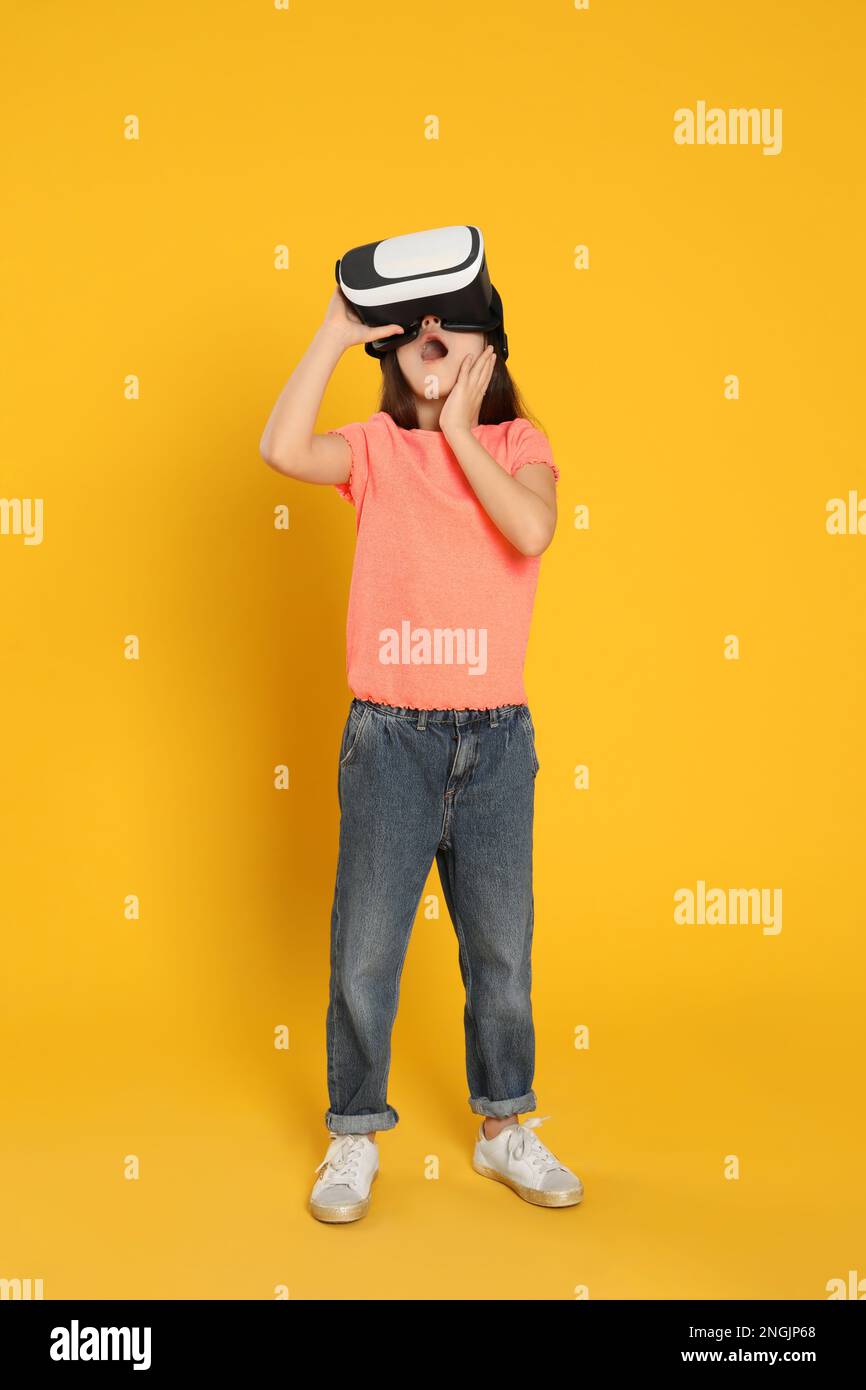 Emotional little girl using virtual reality headset on yellow ...