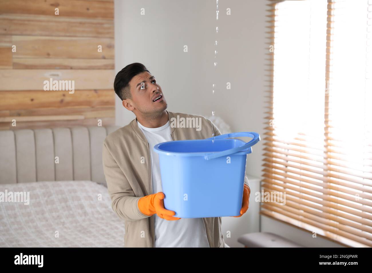 Emotional man collecting water leaking from ceiling in bedroom. Damaged ...
